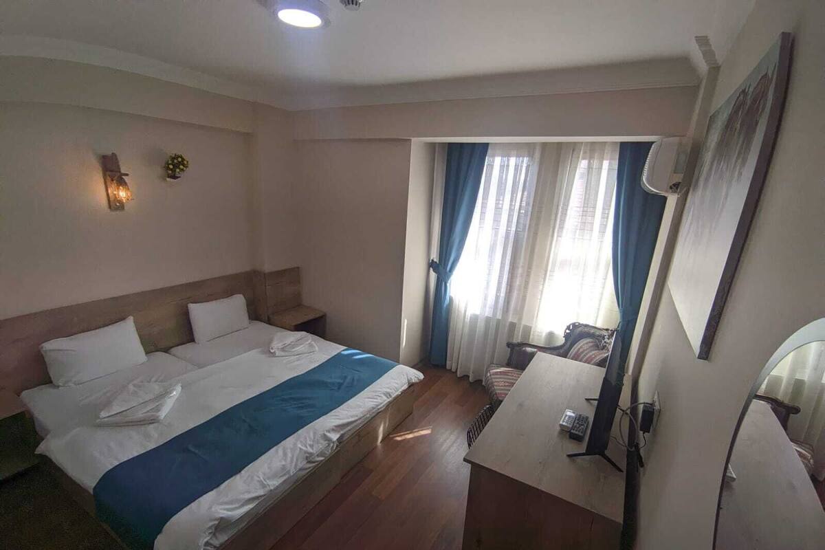 Quarto de hotel com cama, mesa de cabeceira e escrivaninha com cadeira.