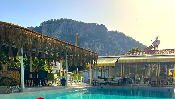 Piscina com borda de pedra, cercada por área de estar externa e montanhas ao fundo.