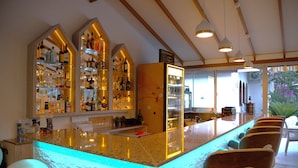 Uma área de bar com balcão, banquetas e prateleiras cheias de garrafas.