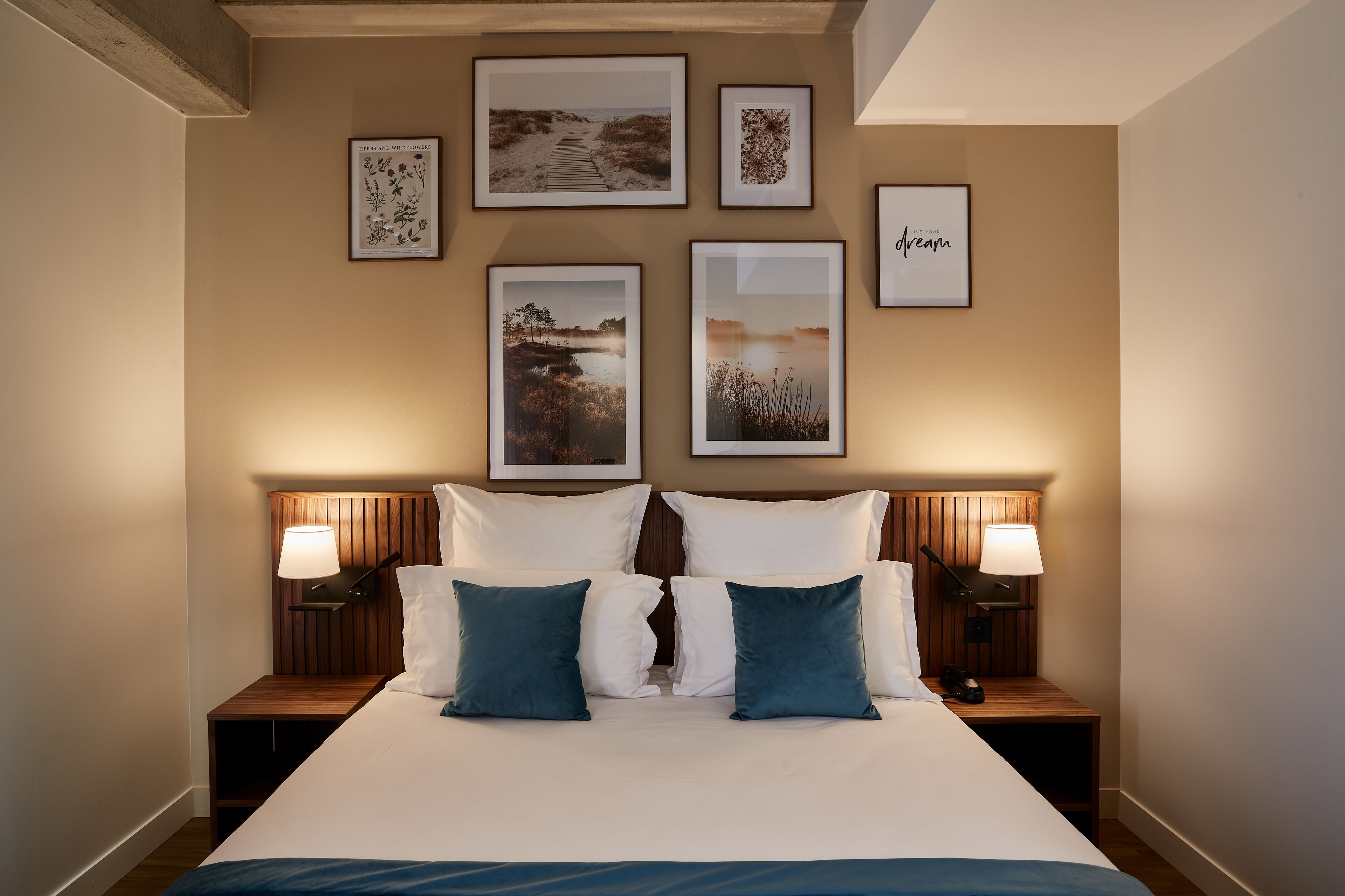 Quarto bem arrumado com uma cama grande, duas mesas de cabeceira com luminárias e quatro quadros na parede.
