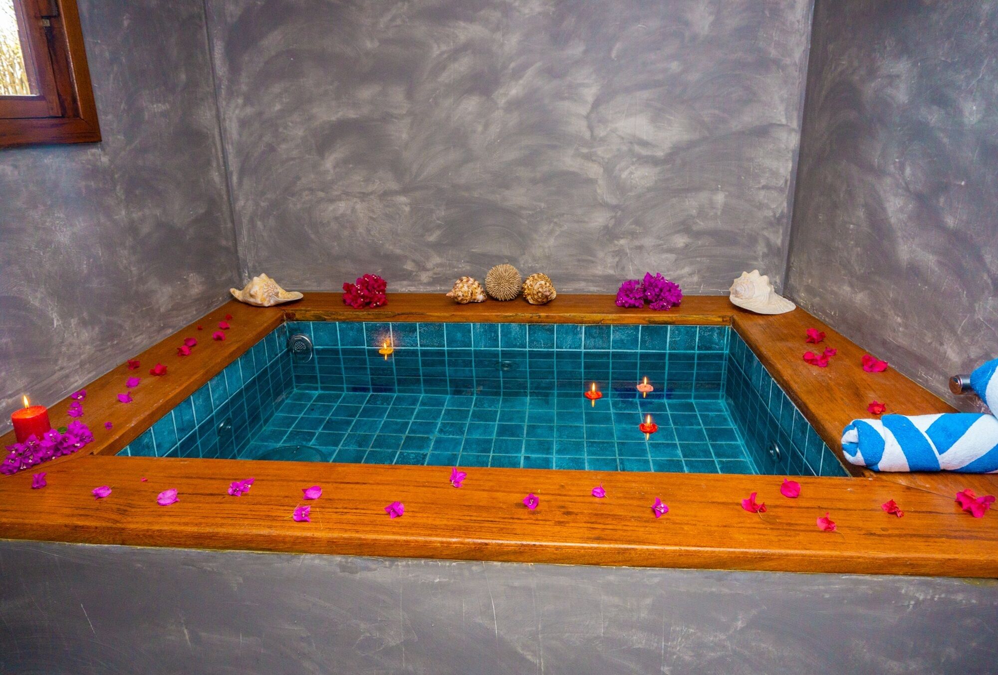 Uma banheira com borda de madeira, azulejos azuis e conchas e flores decorativas.