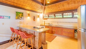 Uma cozinha com ilha central, banquetas de madeira, geladeira e micro-ondas.