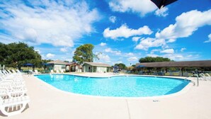 Piscina com espreguiçadeiras e guarda-sóis, cercada por edifícios e árvores.