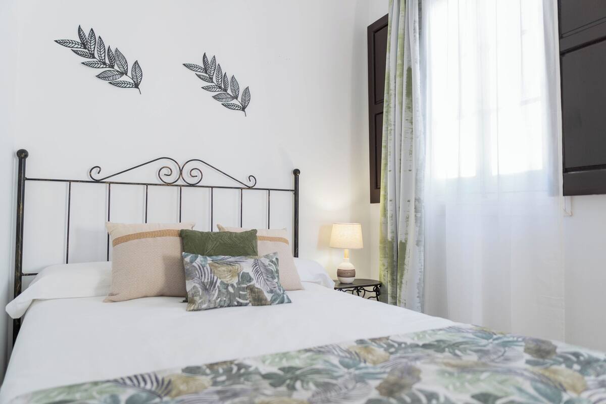 Cama bem arrumada com colcha floral, abajur e duas obras de arte na parede.