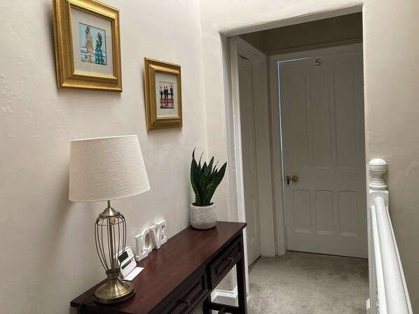 Um corredor com uma mesa, uma luminária, quadros e um vaso de planta.