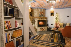 Uma sala de estar aconchegante com lareira, estantes de livros, um pinheiro de Natal e uma área de estar confortável.