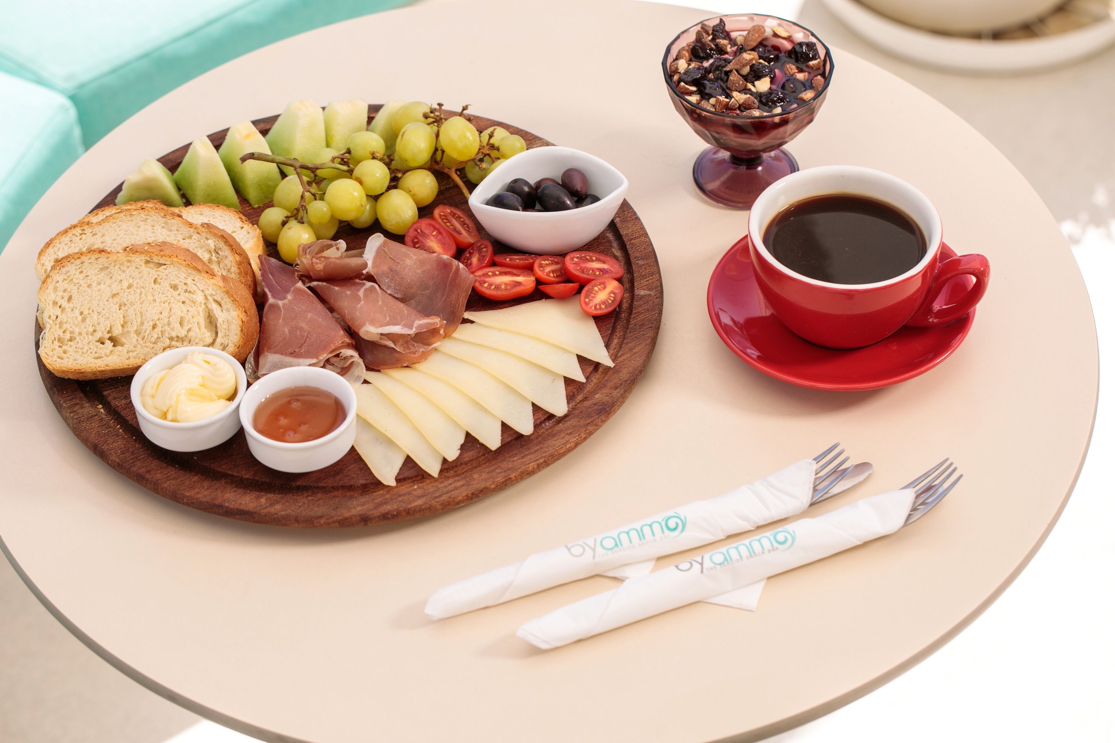 Tábua de madeira com diversos queijos, uvas, azeitonas e tomates, acompanhada de pão e acompanhamentos.