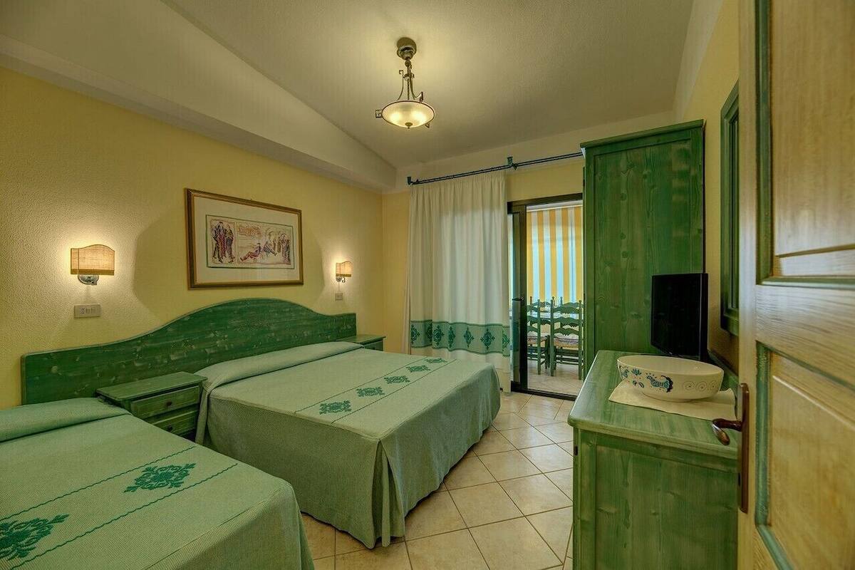 Quarto de hotel com duas camas, uma mesinha com uma tigela, televisão e varanda com uma cadeira.