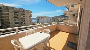 Varanda com mesa e cadeiras, vista para um horizonte urbano com edifícios e um corpo d'água.