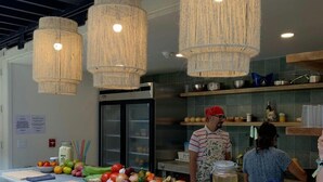 Cozinha com ilha central, cadeiras de madeira e lustres de vime suspensos.