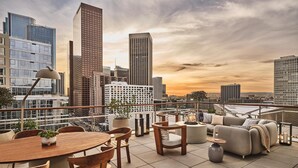 Terraço no telhado com vista para o horizonte da cidade, mobiliado com uma mesa redonda, cadeiras e um sofá.