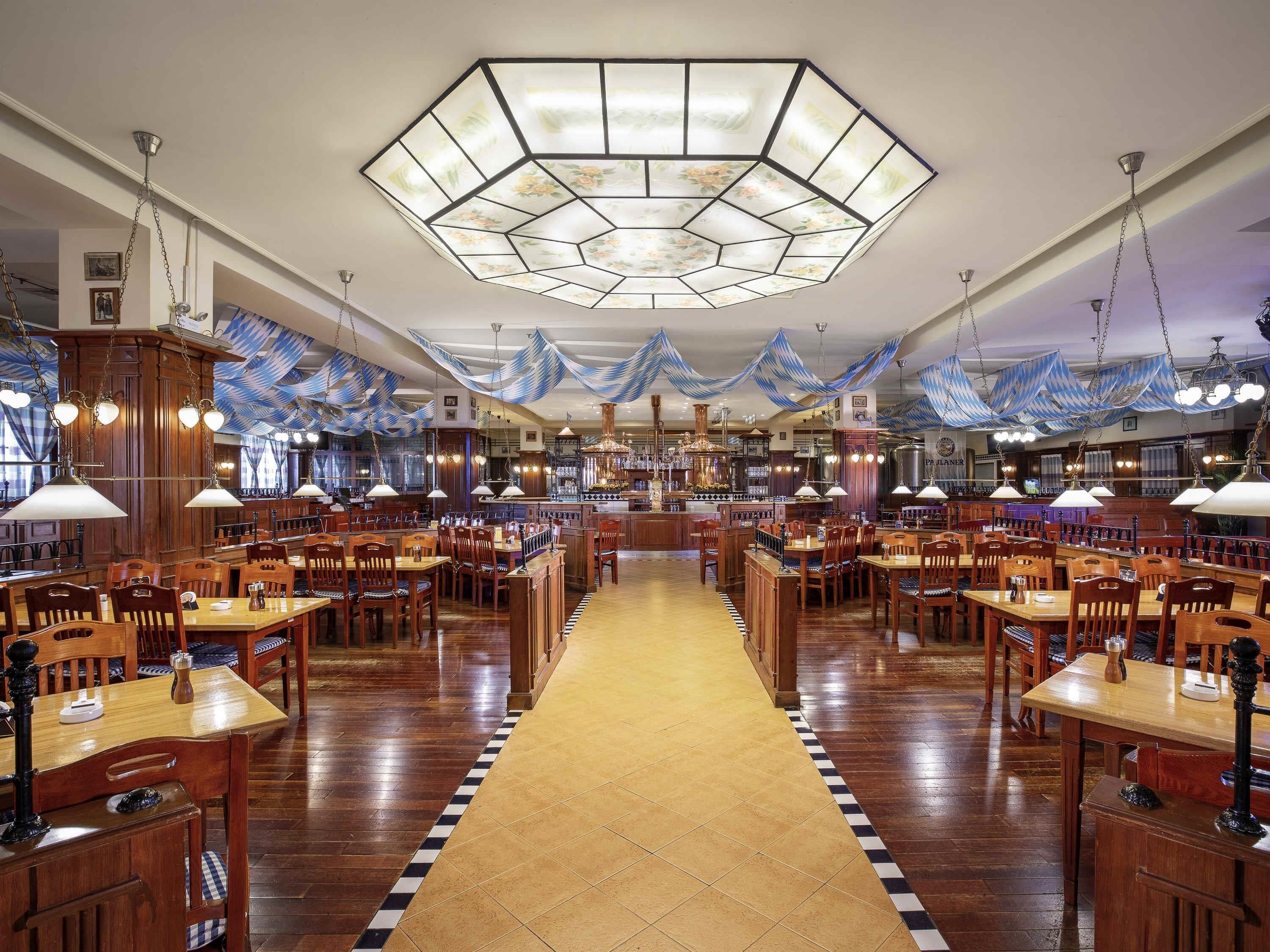 Um restaurante amplo com mesas e cadeiras de madeira, um balcão central e um teto decorativo.