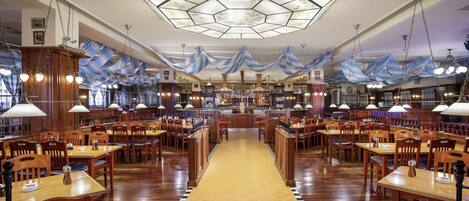 Um restaurante amplo com mesas e cadeiras de madeira, um balcão central e um teto decorativo.