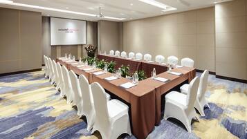 Uma sala de conferências com uma mesa comprida, cadeiras brancas e uma tela de projeção exibindo 'swissotel SHENYANG'.