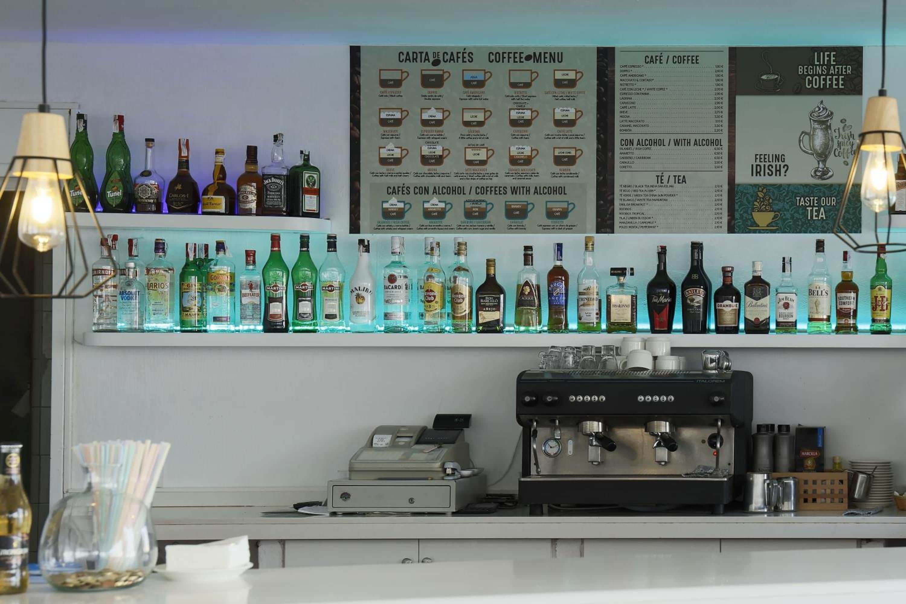 Uma área de bar com cardápio de café, seleção de garrafas de bebidas alcoólicas e máquina de café.