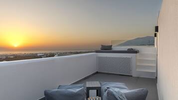 Uma varanda com vista para o pôr do sol, uma mesa pequena e duas cadeiras.