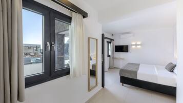 Quarto de hotel moderno com uma janela grande, uma cama, uma mesa de cabeceira e uma televisão fixada na parede.