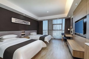 Quarto de hotel com duas camas, uma escrivaninha, televisão e uma janela grande com cortinas.