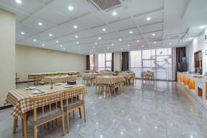 Uma sala de conferências ampla, com várias mesas e cadeiras, janelas grandes e uma área de recepção.