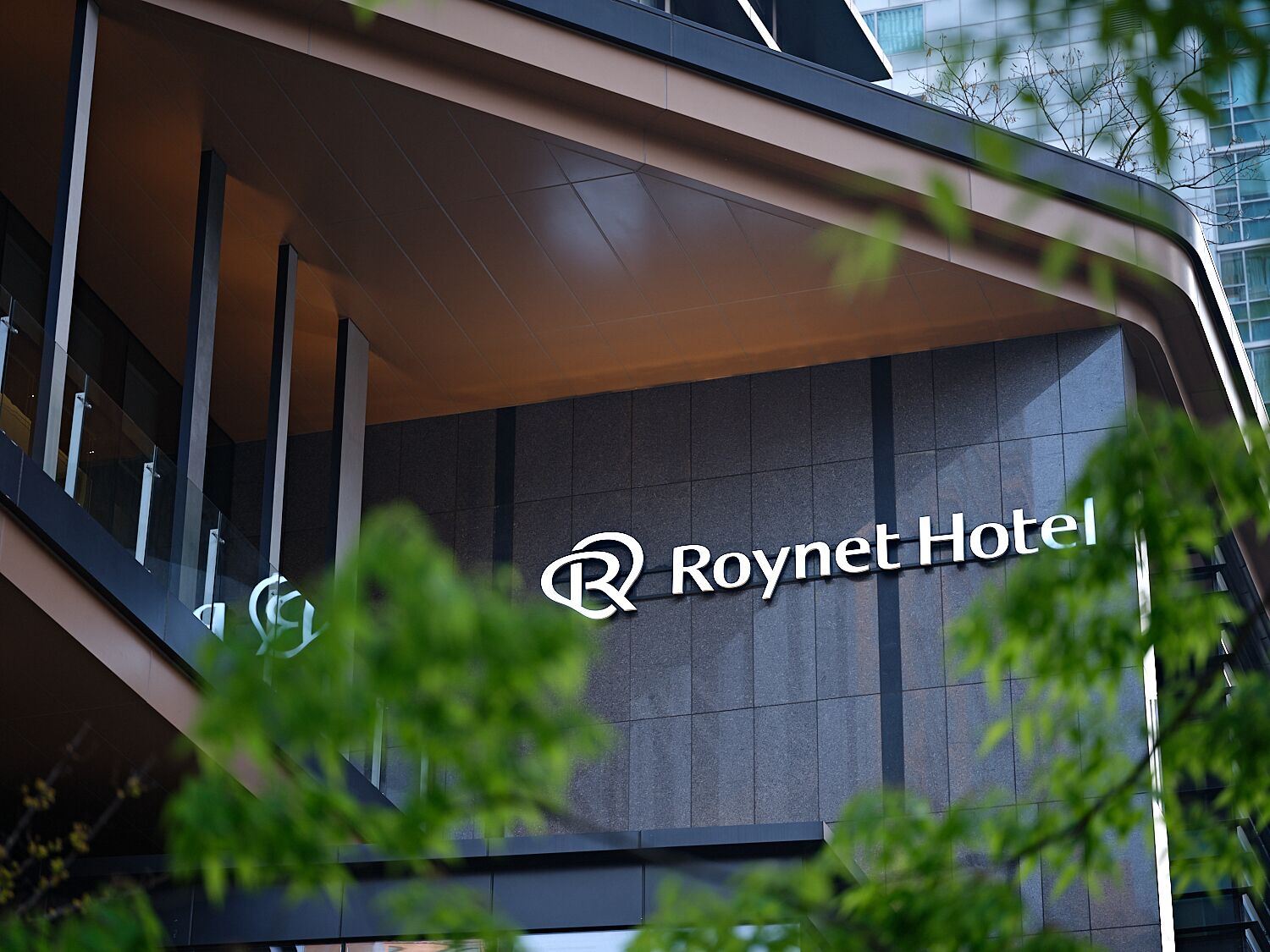 Exterior do Hotel Roynet com design moderno, apresentando um logotipo marcante e fachada elegante.