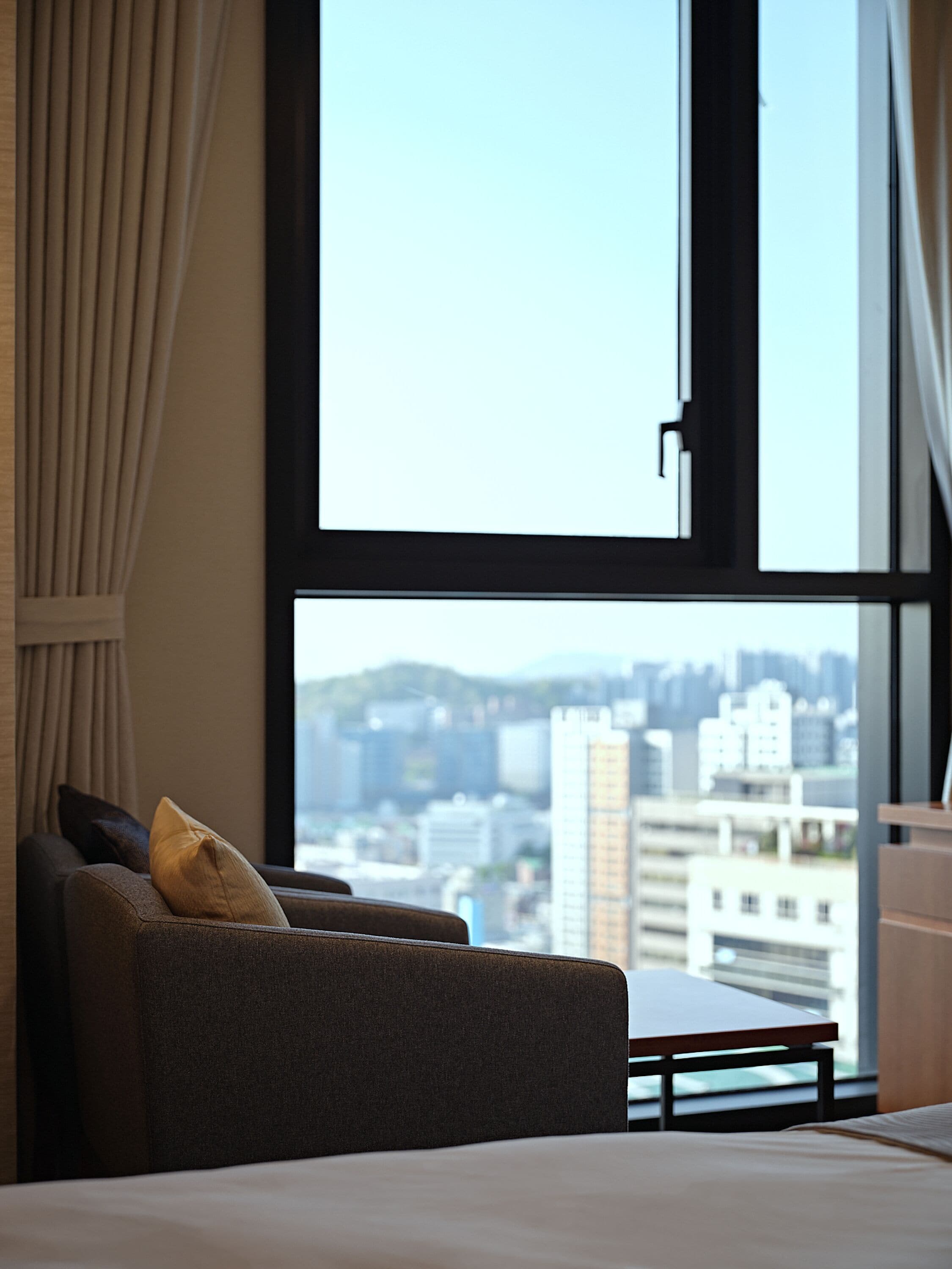 Quarto de hotel com uma janela ampla, um sofá, uma mesinha e uma cama.