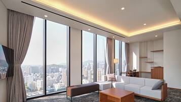 Quarto de hotel moderno com uma janela ampla que oferece vista para a cidade, um sofá, uma mesa de centro e uma TV fixada na parede.