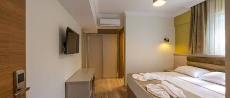 Quarto de hotel com cama, escrivaninha, televisão e guarda-roupa.