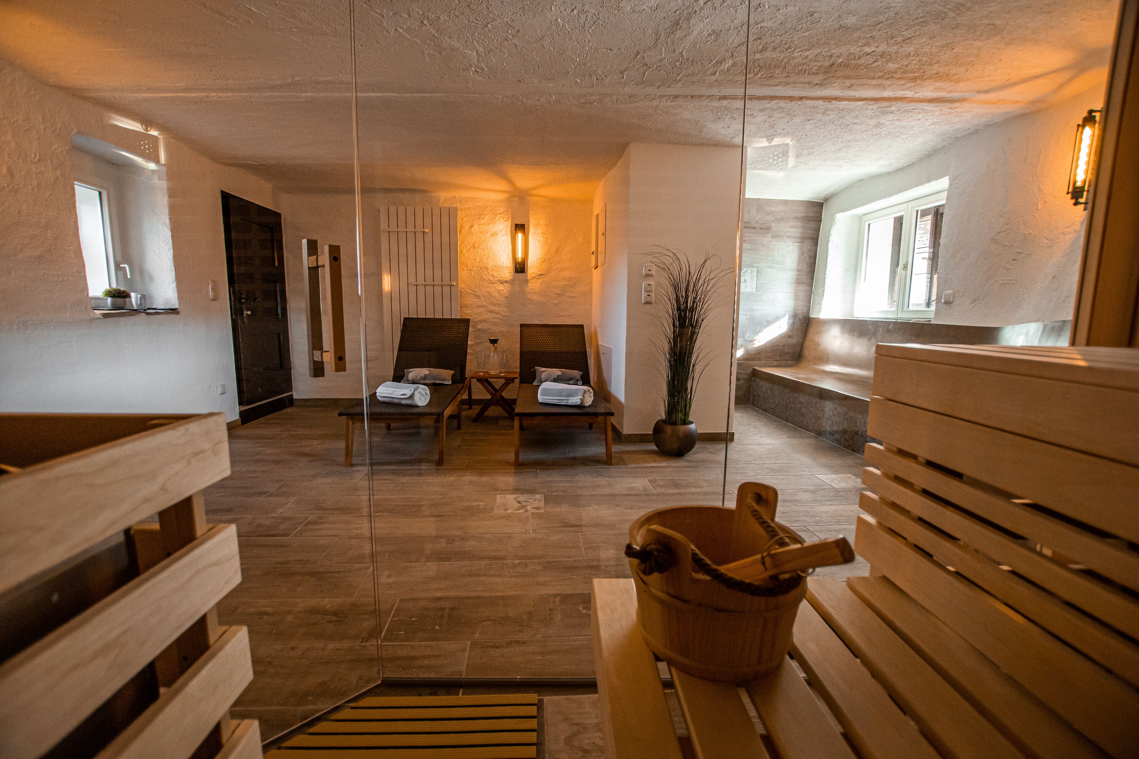 Uma área de spa com bancos de madeira, mesa de massagem e uma grande planta em vaso.