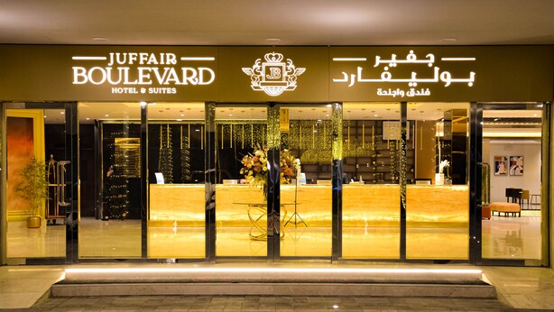 Entrada do Hotel & Suites Juffair Boulevard, com balcão de recepção e divisória de vidro.