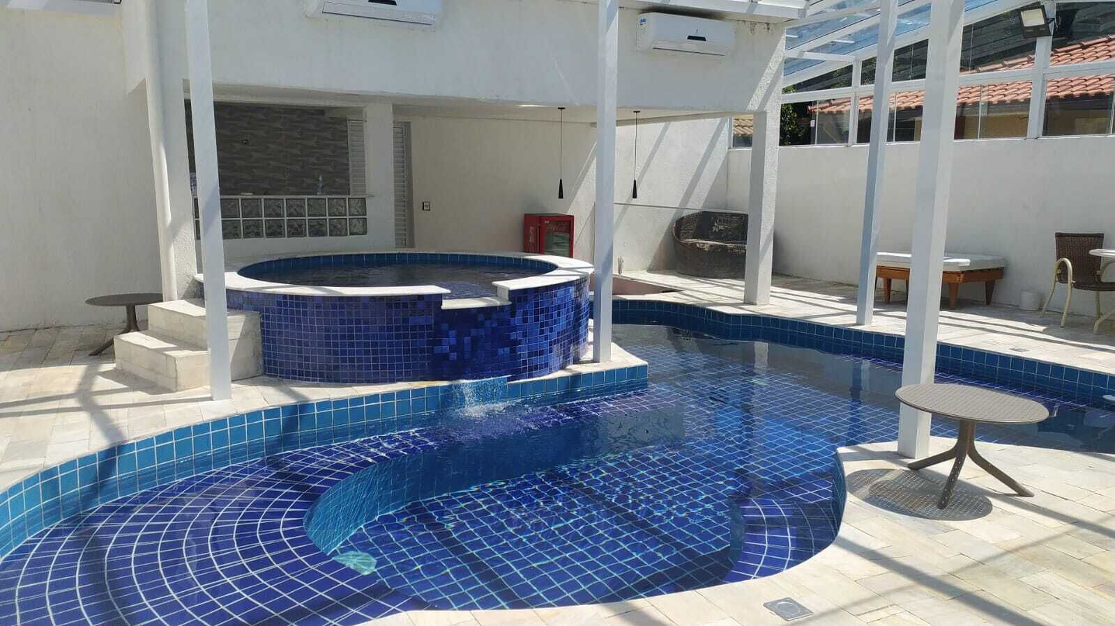 Piscina com hidromassagem, rodeada por um terraço coberto com mesas e cadeiras.