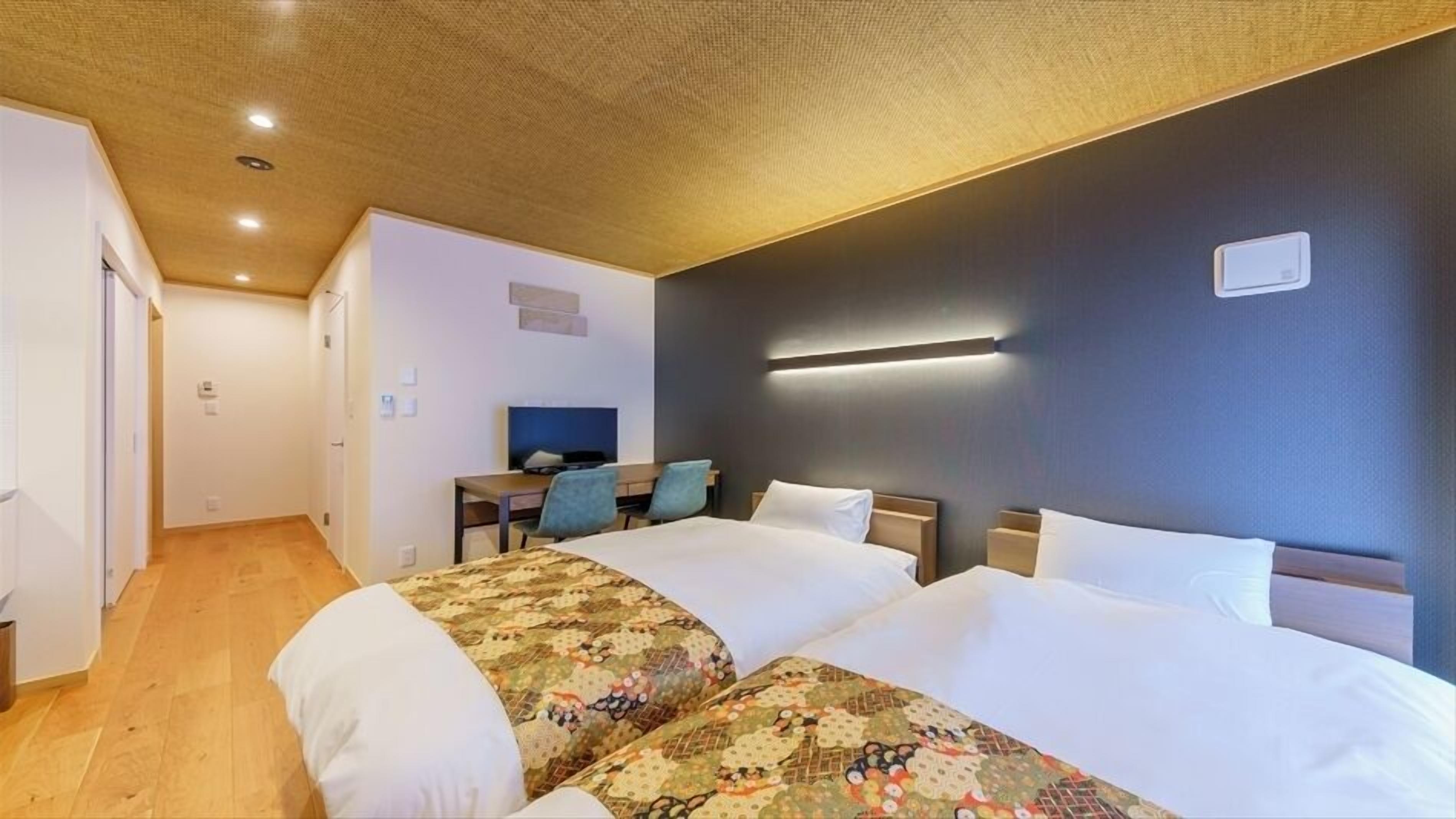 Quarto de hotel com duas camas, uma escrivaninha, uma cadeira e uma televisão.