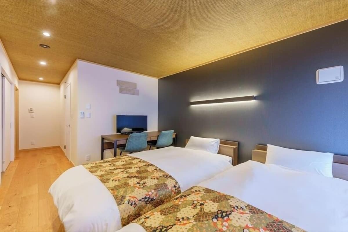 Quarto de hotel com duas camas, uma escrivaninha, uma cadeira e uma televisão.