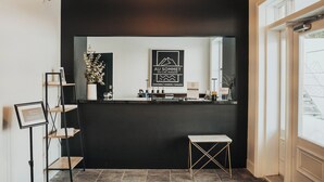 Uma área de recepção com parede preta, uma placa emoldurada, uma pequena mesa e um espelho refletindo o interior.