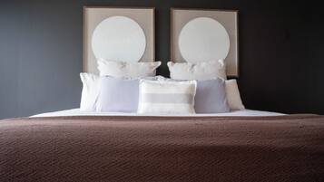 Cama bem arrumada com manta marrom texturizada, almofadas brancas e azul claro, e duas obras de arte emolduradas acima da cama.