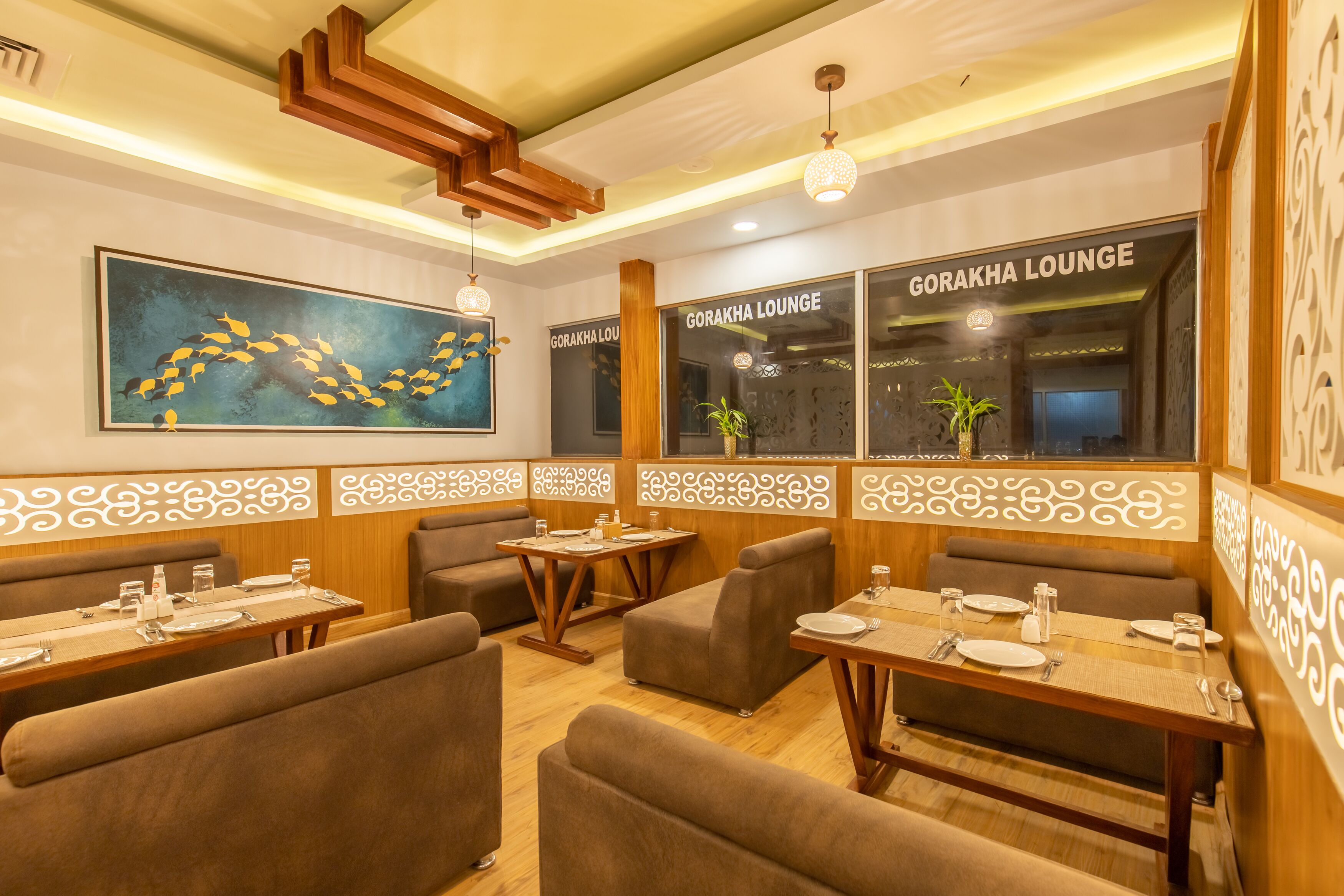 Interior de restaurante com mobiliário de madeira, mesas postas com pratos e copos, painéis decorativos na parede e uma pintura grande de peixes amarelos.