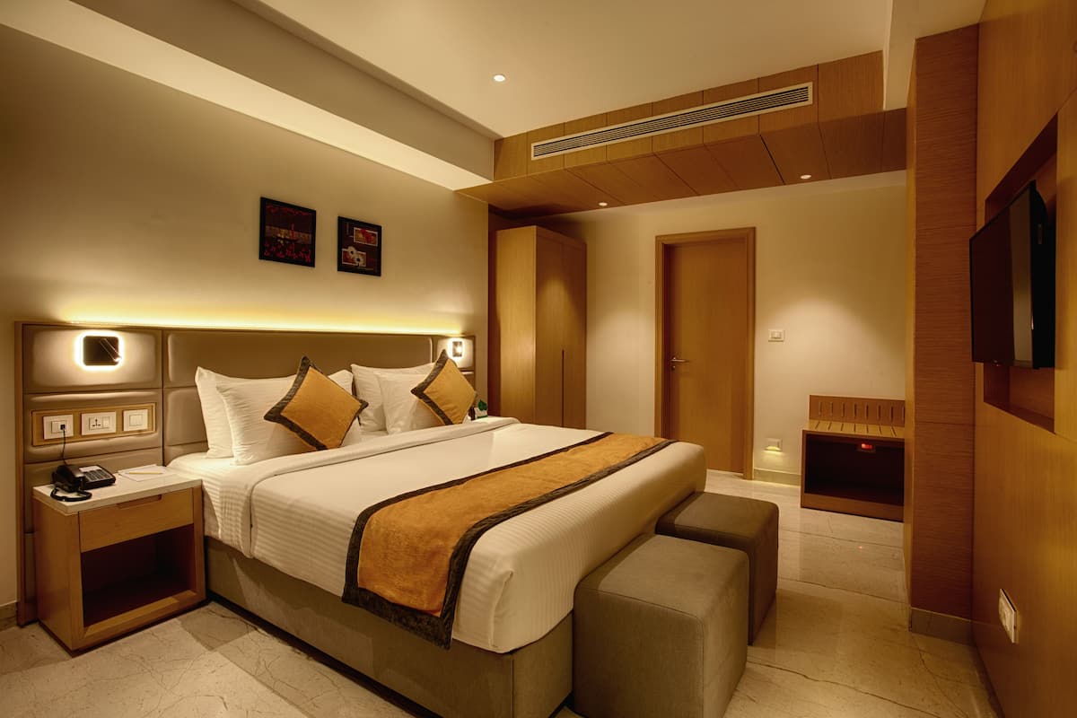 Quarto de hotel moderno com uma cama grande, mesas de cabeceira, televisão de tela plana e um banco embutido.