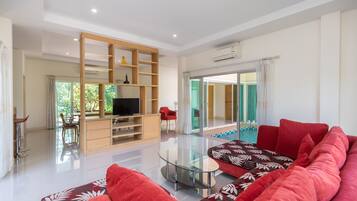 Uma sala de estar moderna com uma mesa de centro de vidro, sofás vermelhos, um móvel para entretenimento de madeira e uma TV.