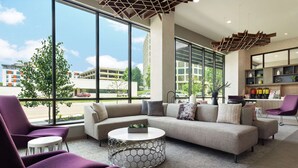 Uma sala de estar moderna com sofá seccional, poltronas roxas, uma mesa de centro redonda e grandes janelas com vista para a rua e edifícios.