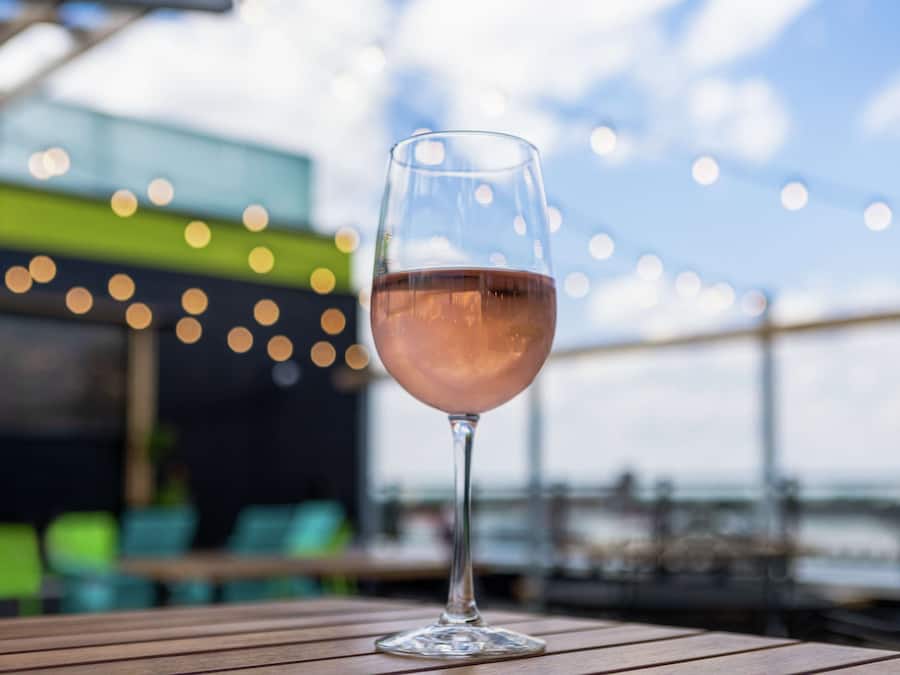 Um copo de vinho rosé sobre uma mesa de madeira, com um fundo desfocado de um restaurante ou bar.