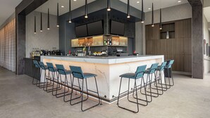 Uma área de bar moderna com balcão de mármore, vários bancos altos e uma variedade de garrafas e copos.