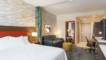 Quarto de hotel com uma cama grande, um sofá, uma escrivaninha e uma cadeira.