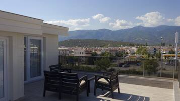 Uma varanda com mesa e cadeiras, com vista para uma cidade e montanhas ao longe.