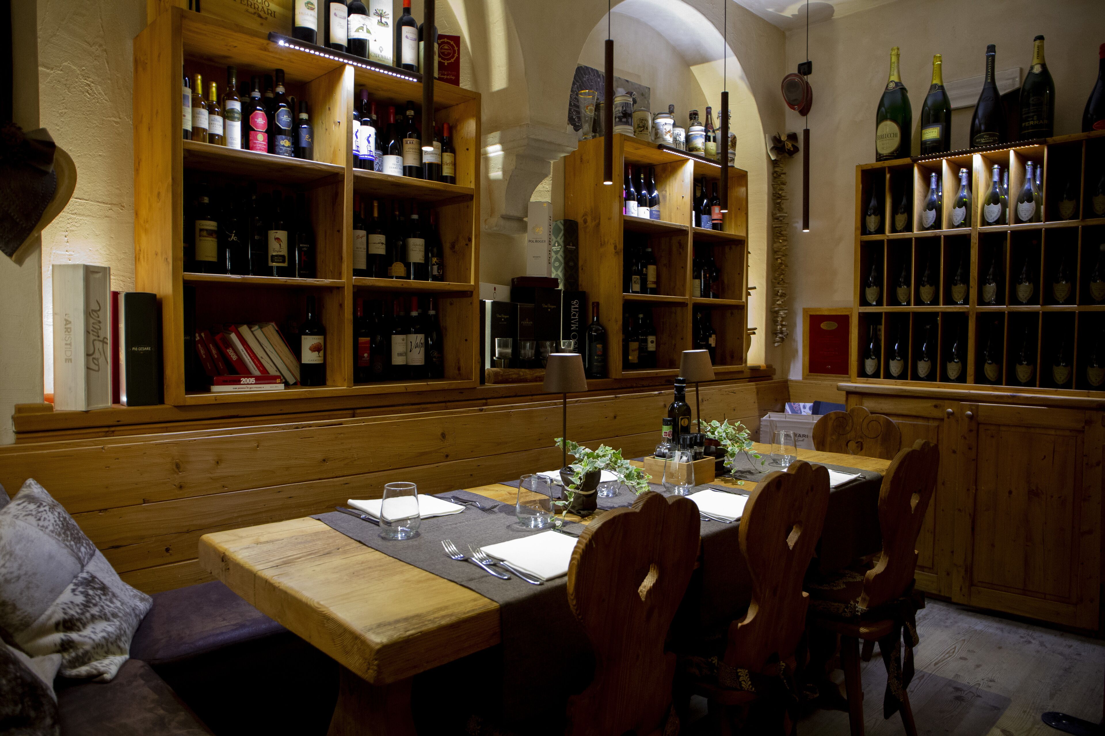 Uma área de refeições com mesas e cadeiras de madeira, cercada por prateleiras cheias de garrafas de vinho.