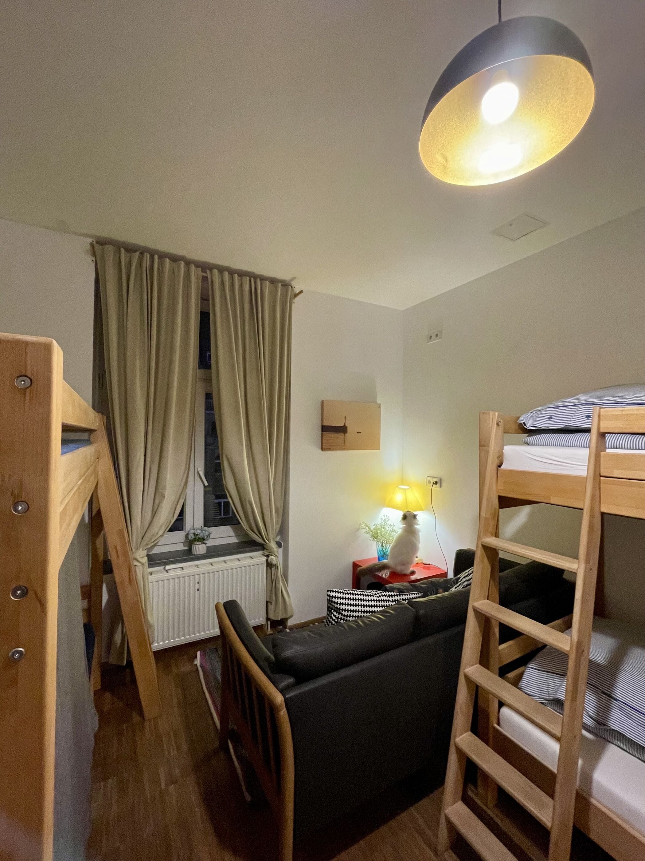 Quarto compacto com beliches, um pequeno sofá, escrivaninha e janela com cortinas.