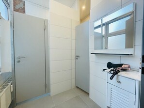 Casa de banho com paredes revestidas a azulejos brancos, um espelho sobre a pia e um secador de cabelo no balcão.
