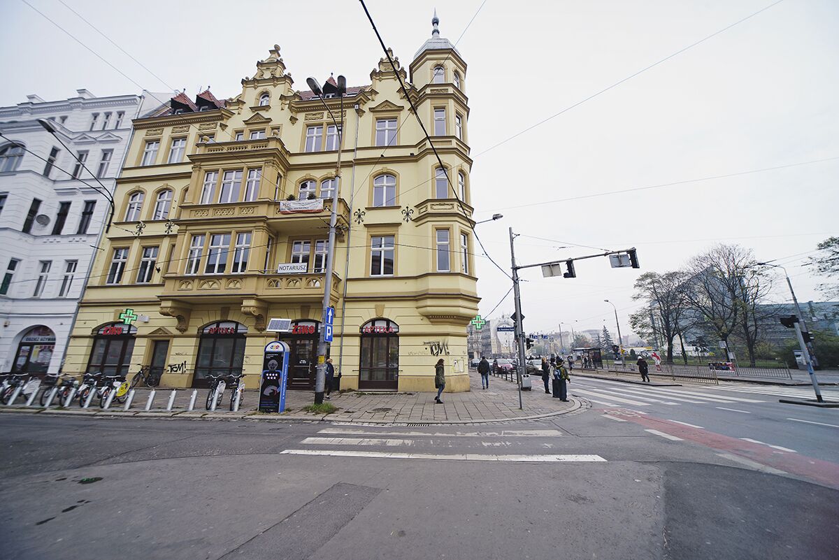 Um edifício histórico com arquitetura elaborada, uma farmácia e uma faixa de pedestres.