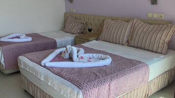 Quarto de hotel com duas camas, cada uma com colcha listrada em rosa e branco, uma cama grande com padrão semelhante e uma mesinha com uma taça de vinho.