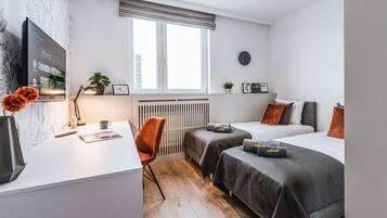 Quarto de hotel moderno com uma janela grande, uma escrivaninha com computador, duas camas e um radiador.