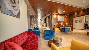 Um hall moderno com um sofá vermelho, poltronas azuis e uma poltrona amarela. Há vasos decorativos com flores sobre uma mesa.