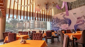 Um restaurante com mesas cobertas por toalhas laranja, cadeiras de madeira e um mural na parede.